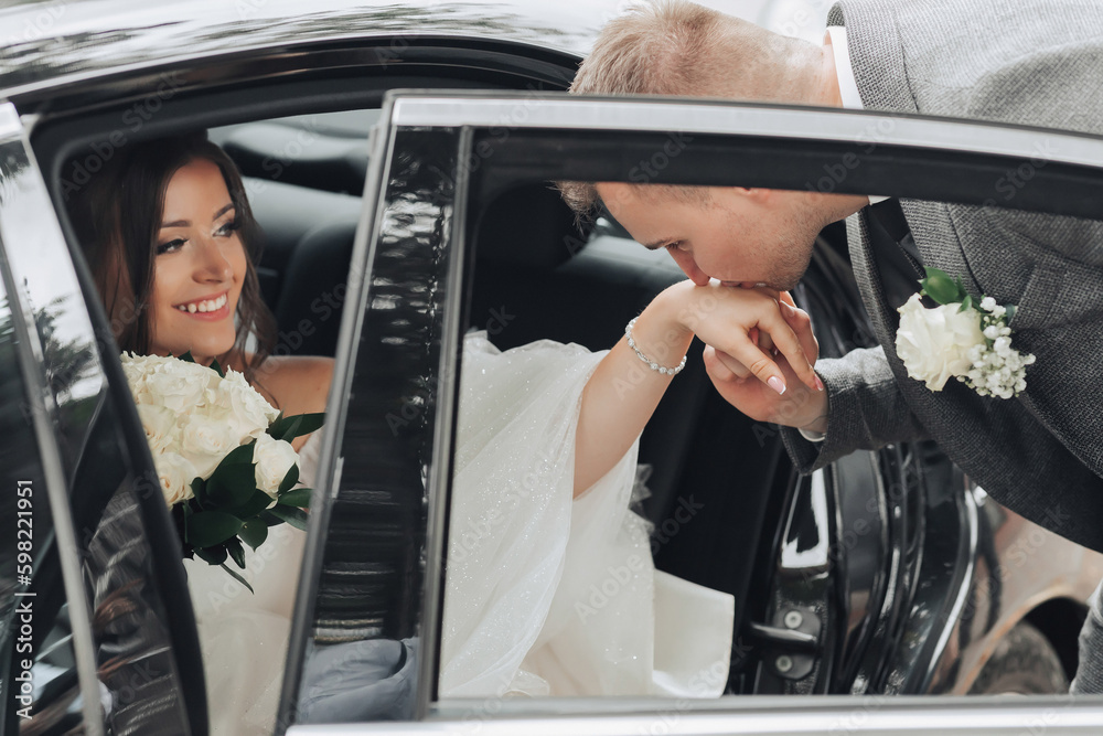 Wedding photo. The bride sits in a black car with a smile, the groom ...
