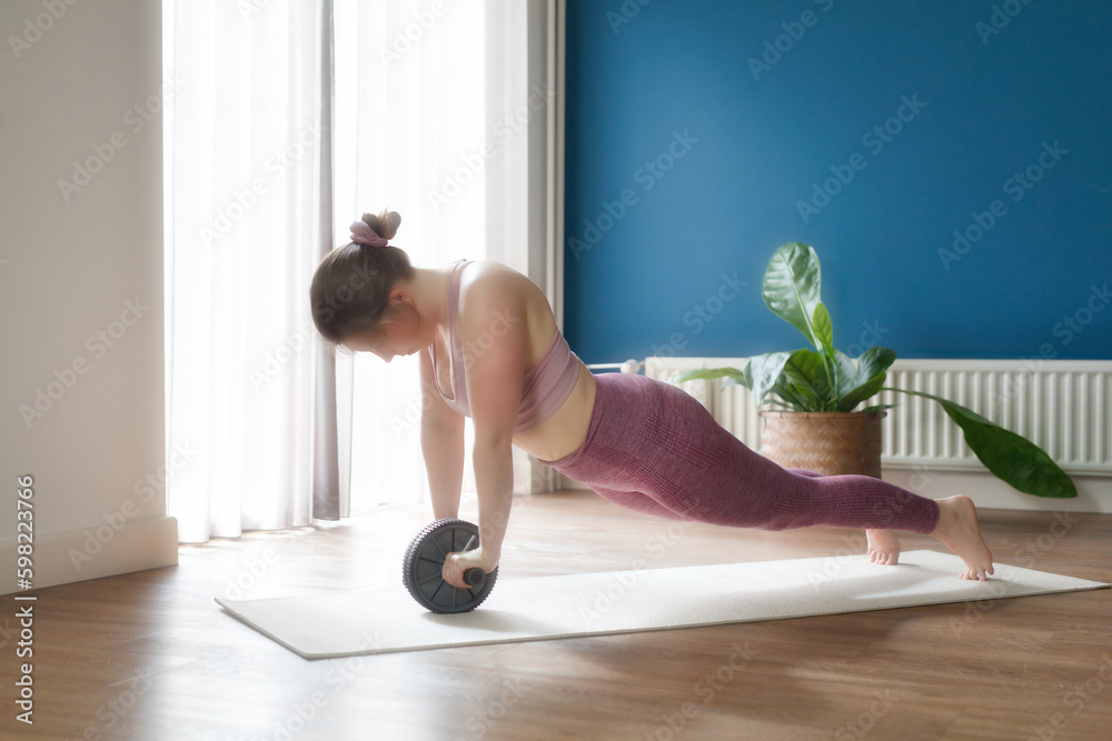 Beautiful strong woman in sportswear is working out with exercise wheel ...