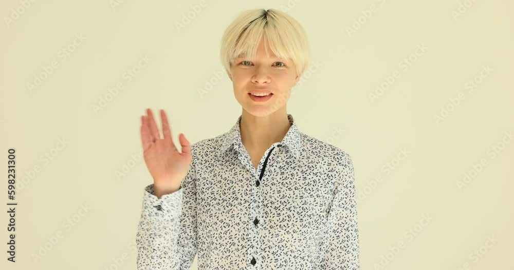 Stylish blonde woman waves hand to greet and smiles nicely. Young ...
