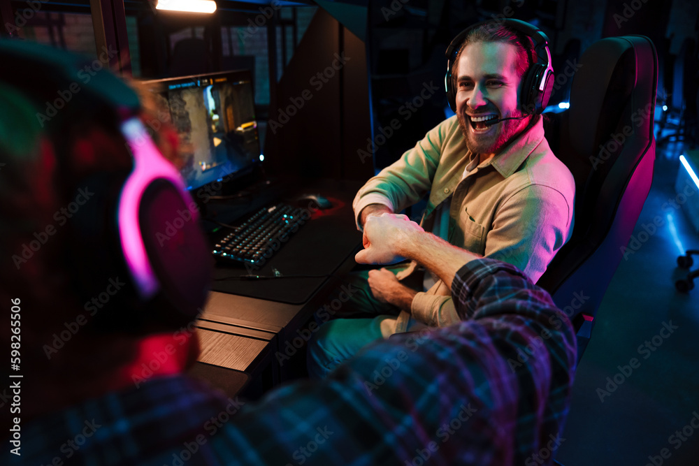 Two male gamers giving fist bump while playing video game together in ...