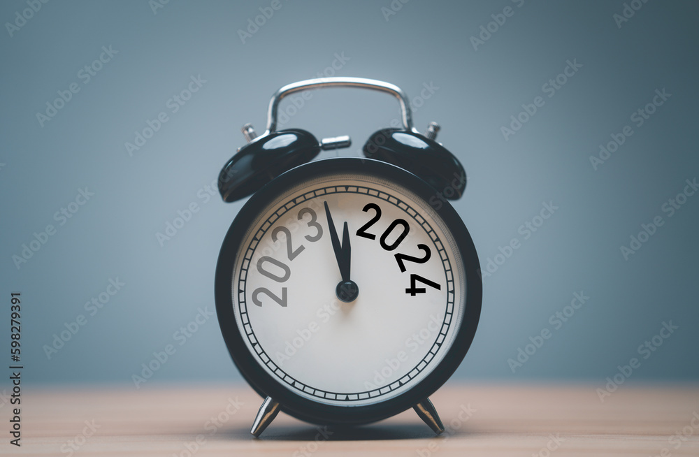 2023 and 2024 on black alarm clock on wooden table with copy space for ...