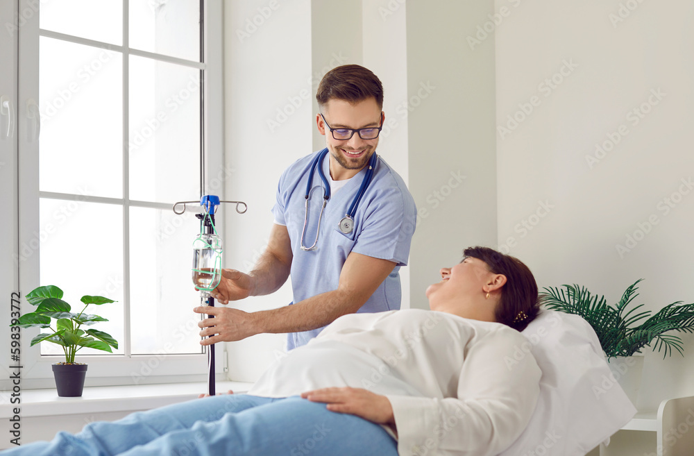 Male nurse gives an IV line to a female patient. Friendly young man in ...