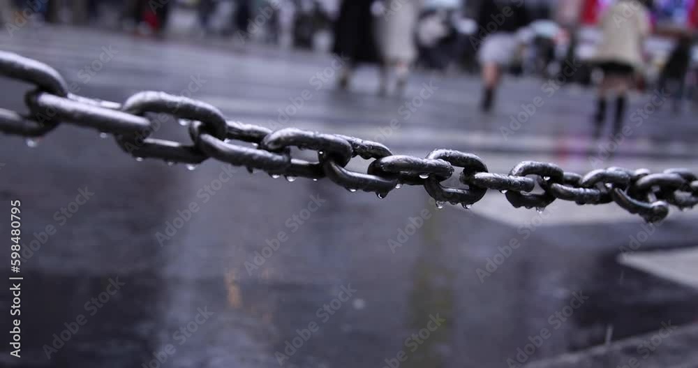 A silver chain behind walking people at the SHIBUYA crossing rainy day ...