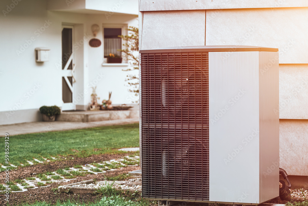 An air conditioner outdoor unit outside of a house in the grass. Modern ...