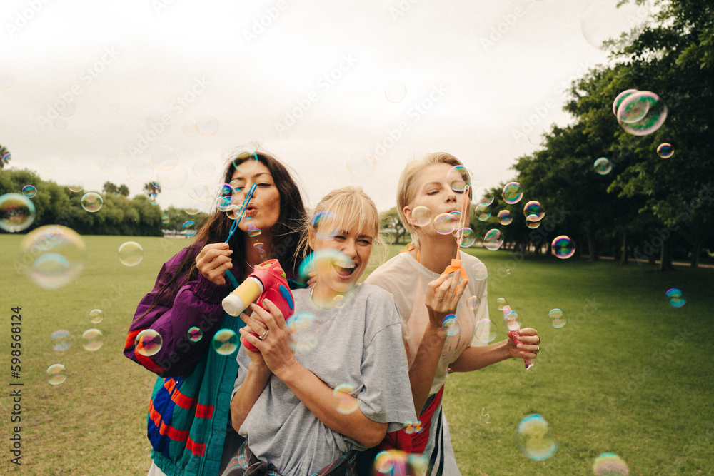 Friends enjoy blowing bubbles while hanging out together in a park ...