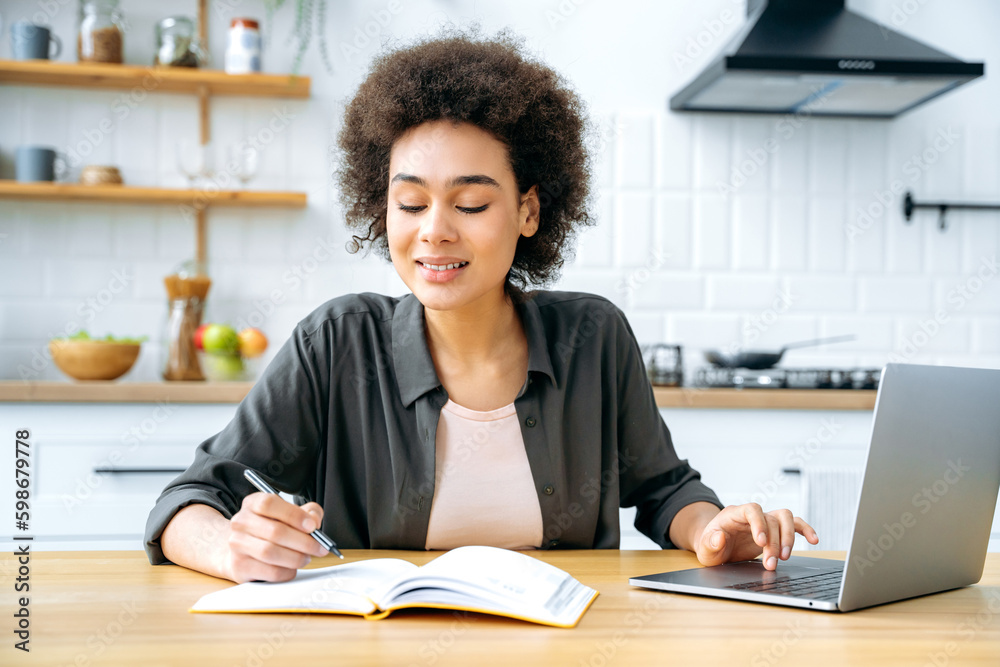 Remote work or education. Positive african american girl with short curly hair, sit at a table ...