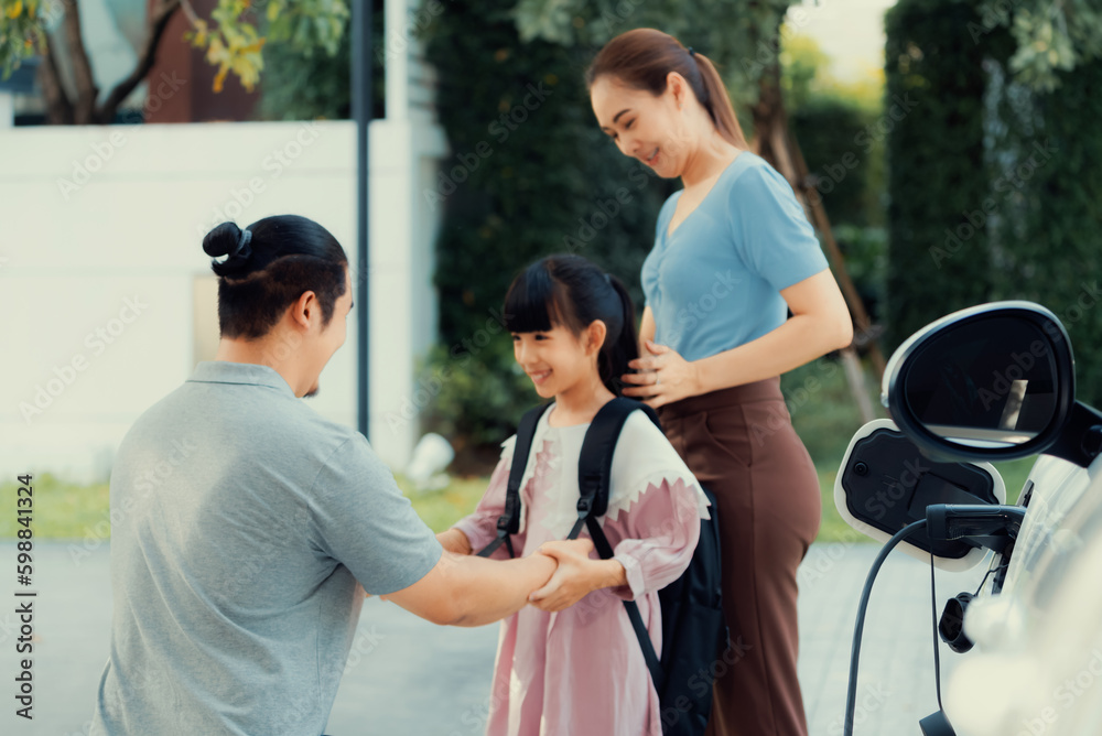 Progressive young parents and daughter with electric vehicle and home ...