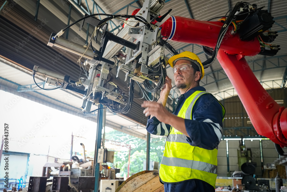 Male technician programs a robot arm with a digital tablet and assembly ...