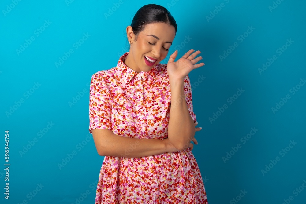 Overjoyed successful beautiful woman wearing floral dress over blue ...