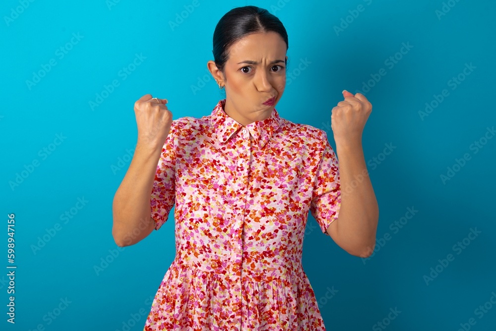 Irritated beautiful woman wearing floral dress over blue studio ...