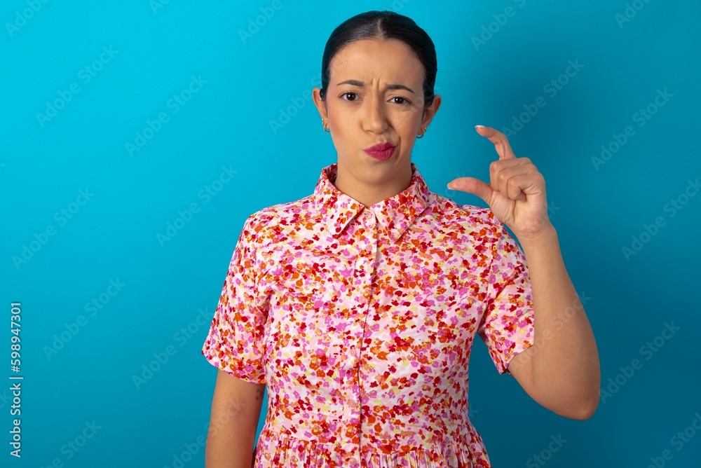 Displeased beautiful woman wearing floral dress over blue studio ...