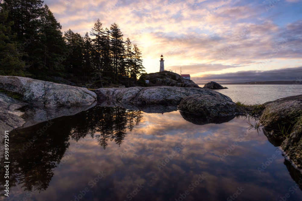Sunrise over a tall lighthouse situated on a rugged rocky coast ...