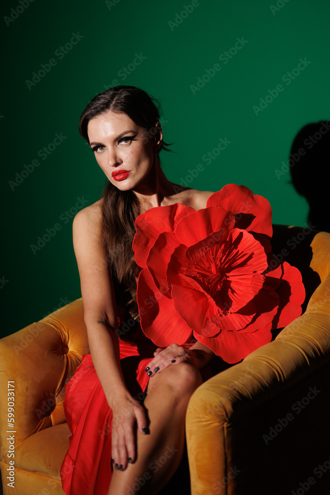 Pinup girl sitting in yellow armchair in red dress with flower ...