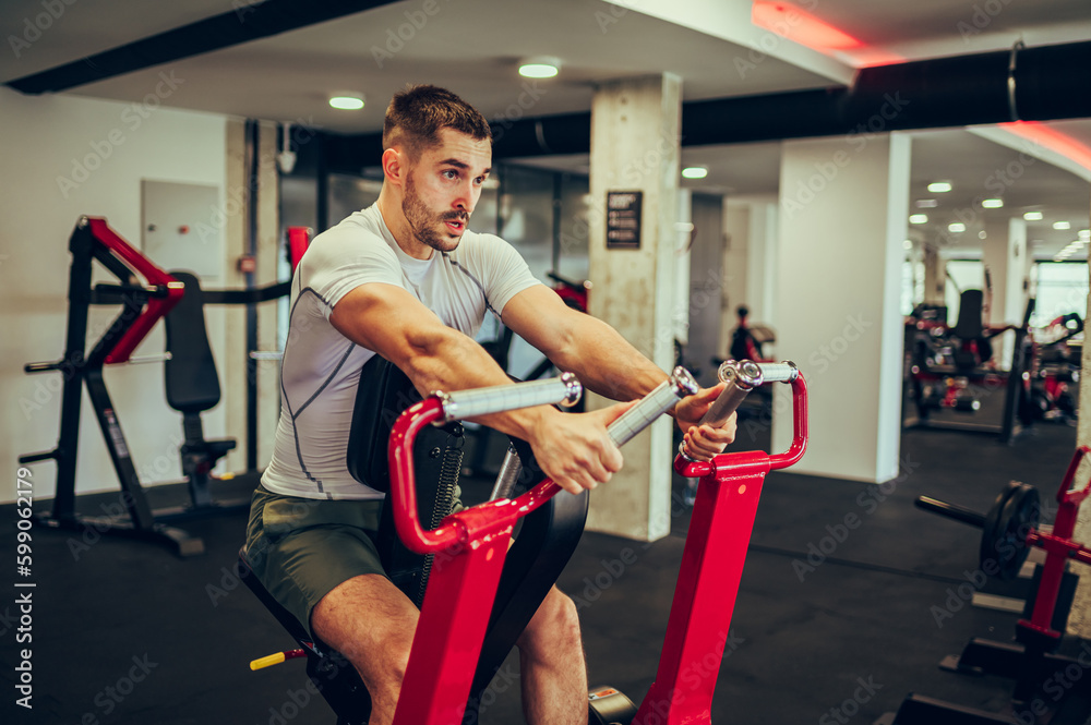 A focused sportsman with big muscles is exercising on a machine in a ...