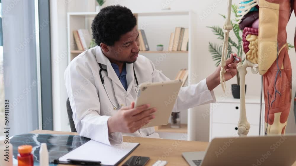 Confident multicultural adult in lab coat pointing at femur of human ...