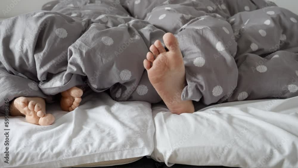 Slow motion closeup of couple's feet hiding under the blanket on a cozy ...