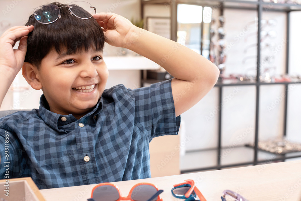Indian child boy choosing glasses in optical store, holding glasses ...