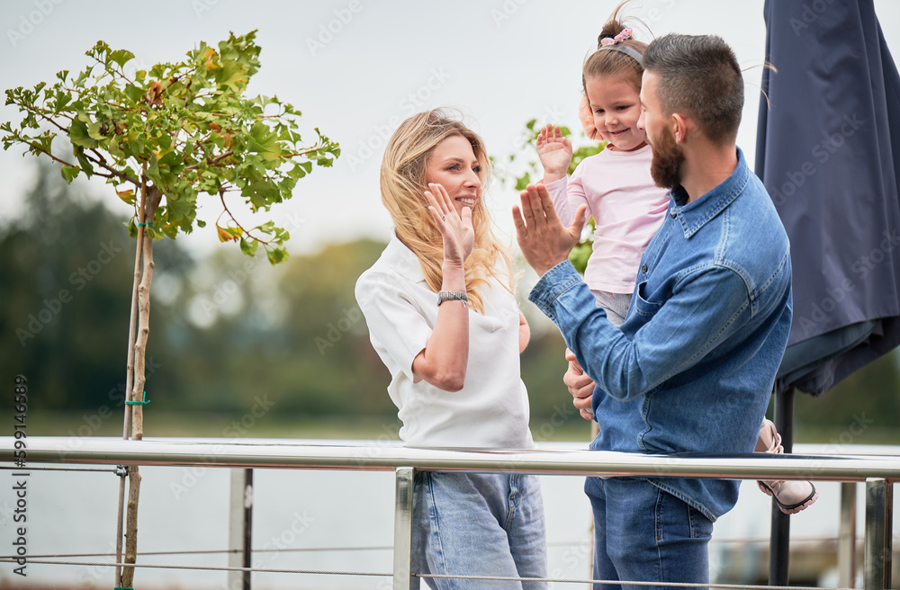 Cheerful woman, man and little girl standing near green tree and ...