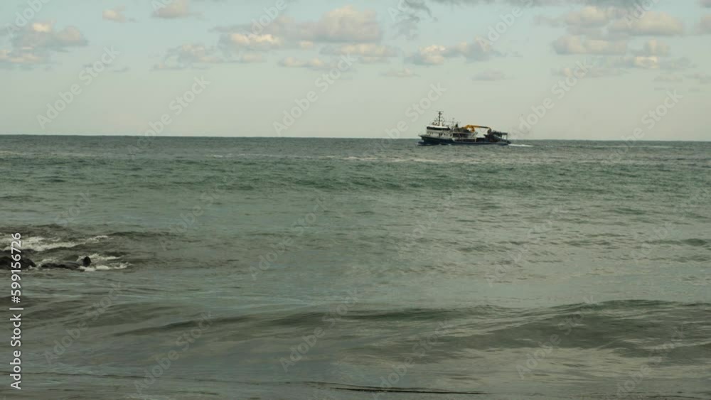 A fishing boat is sailing on the waves not far from the shore. The sea ...