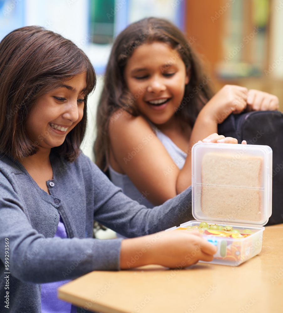 Opening her lunch in the cafeteria. Two young school girls sitting in ...