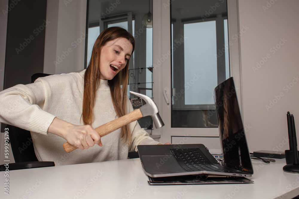 A woman with a hammer wants to break a laptop. Failure at work. Hard ...