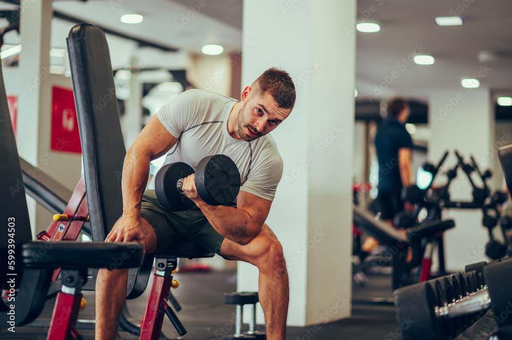 A strong sportsman with big muscles is pumping biceps in a gym while ...