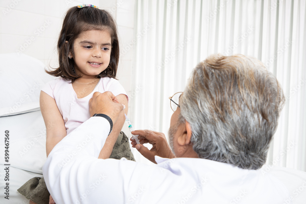 Senior Indian man pediatrician performs a vaccination of a little girl ...