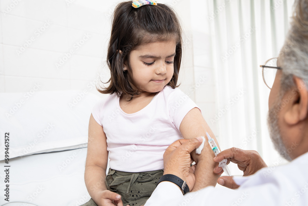 Senior Indian man pediatrician performs a vaccination of a little girl ...