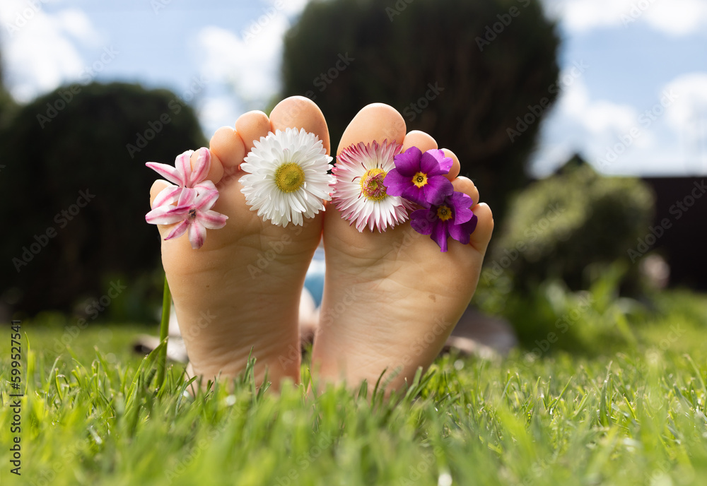 child's bare feet lie on bright juicy green grass. flowers of daisies ...