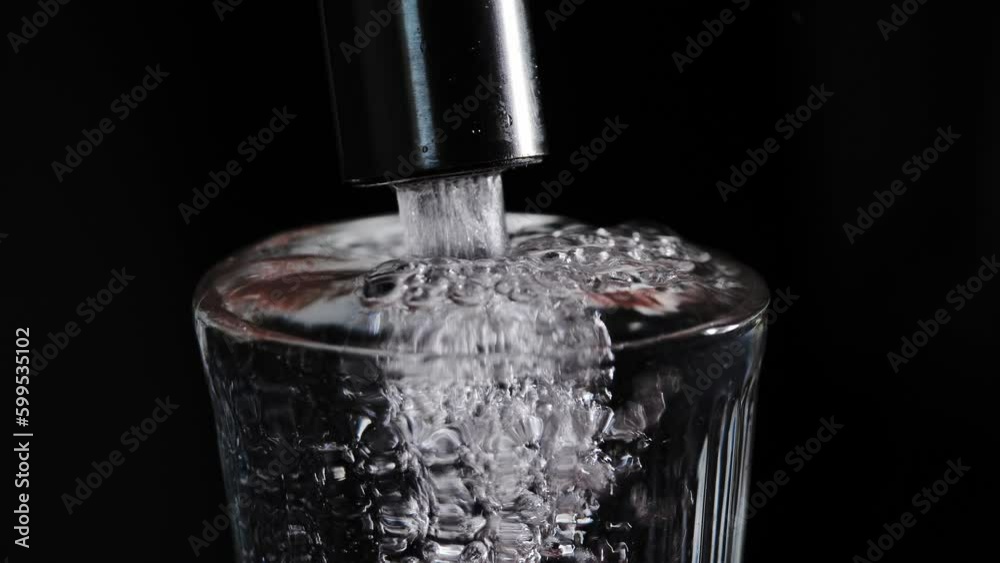 to drink water, filling glass by tap water. Black background. Fresh and ...