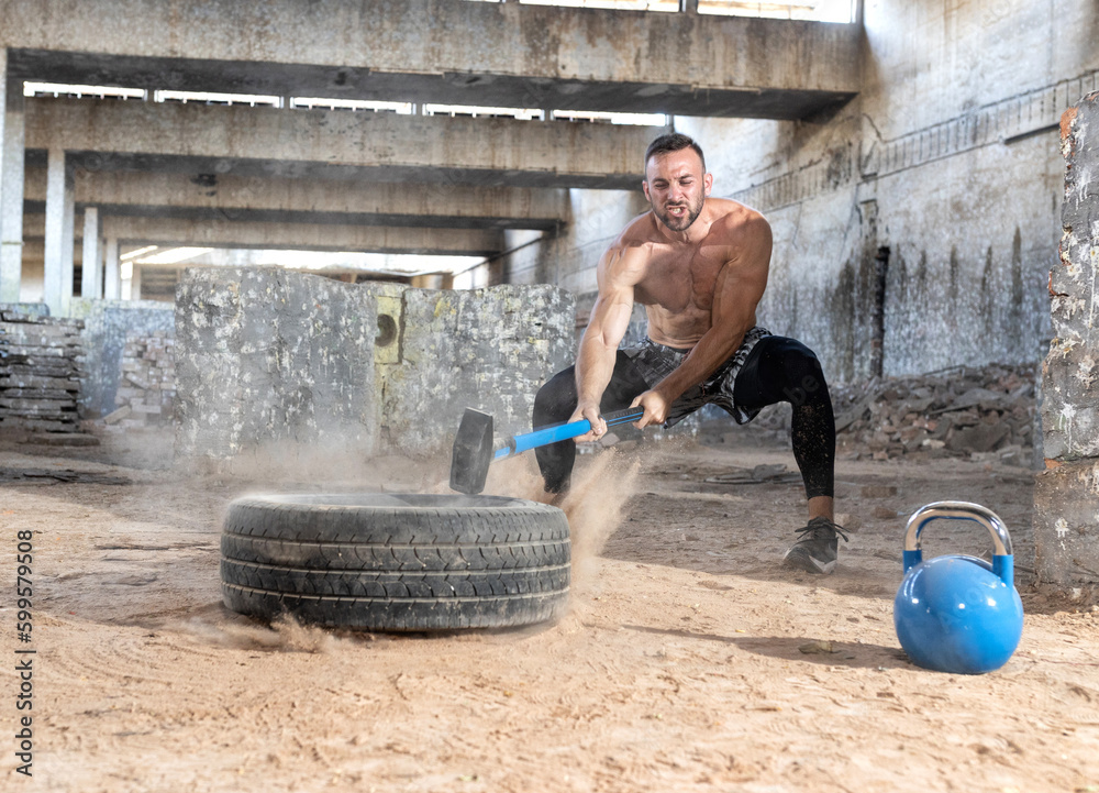 Big, strong and ripped young handsome muscular man hitting a truck tire ...