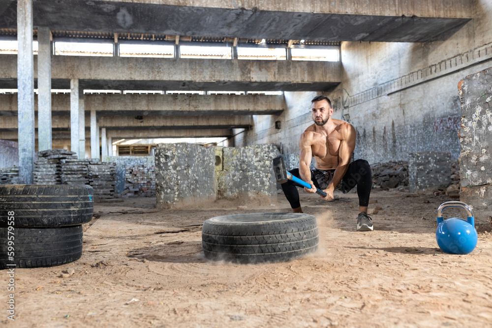 Big muscular ripped guy swinging a hammer against the truck tire ...