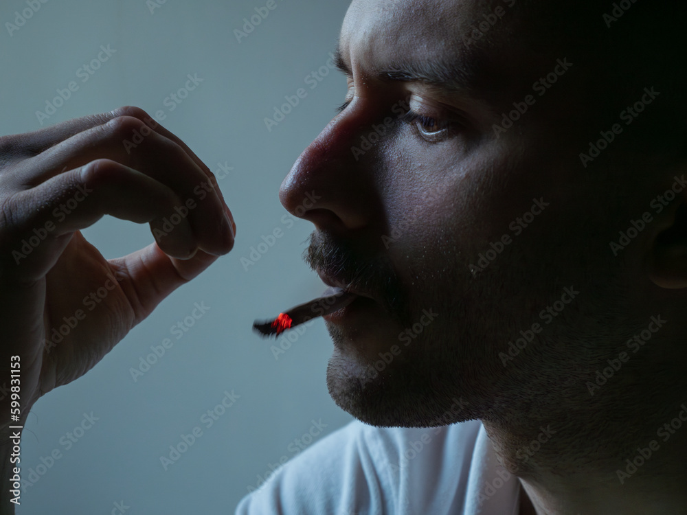 Silhouette of a smoker with a cigarette smokes alone in a dark room ...