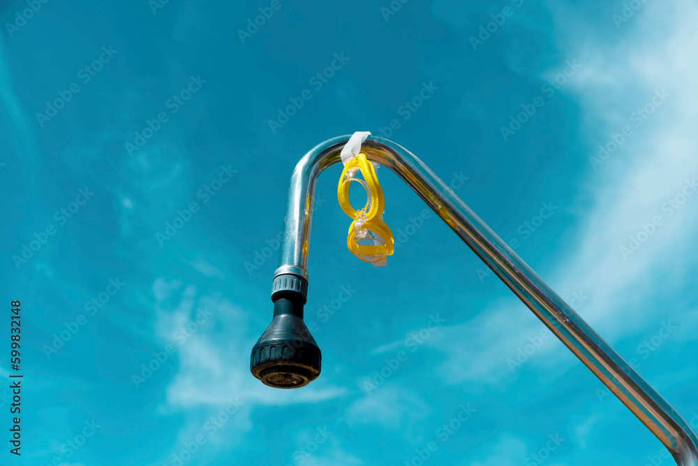 Yellow pool goggles hanging from a pool shower with blue sky in the ...