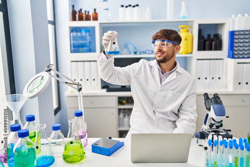 Young arab man scientist using laptop measuring liquid at laboratory ...