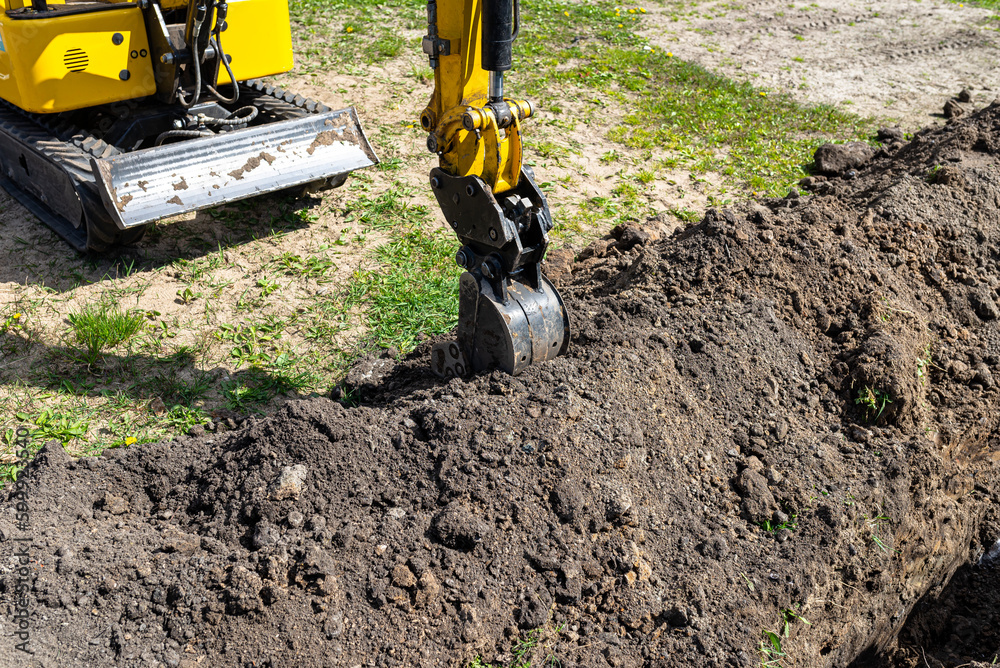 Mini digger digging a hole in the garden along the fence to the ...
