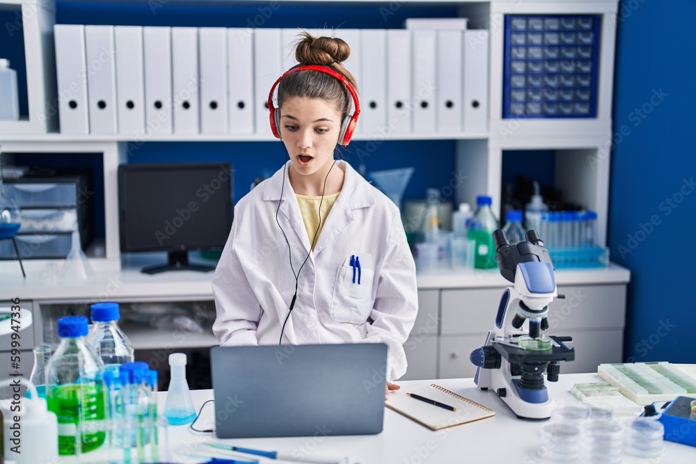 Teenager girl working at scientist laboratory scared and amazed with ...