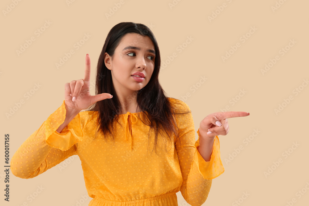Young woman showing loser gesture on beige background Stock Photo ...