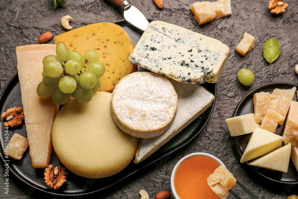 Tray with different types of tasty cheese and grapes on dark background ...