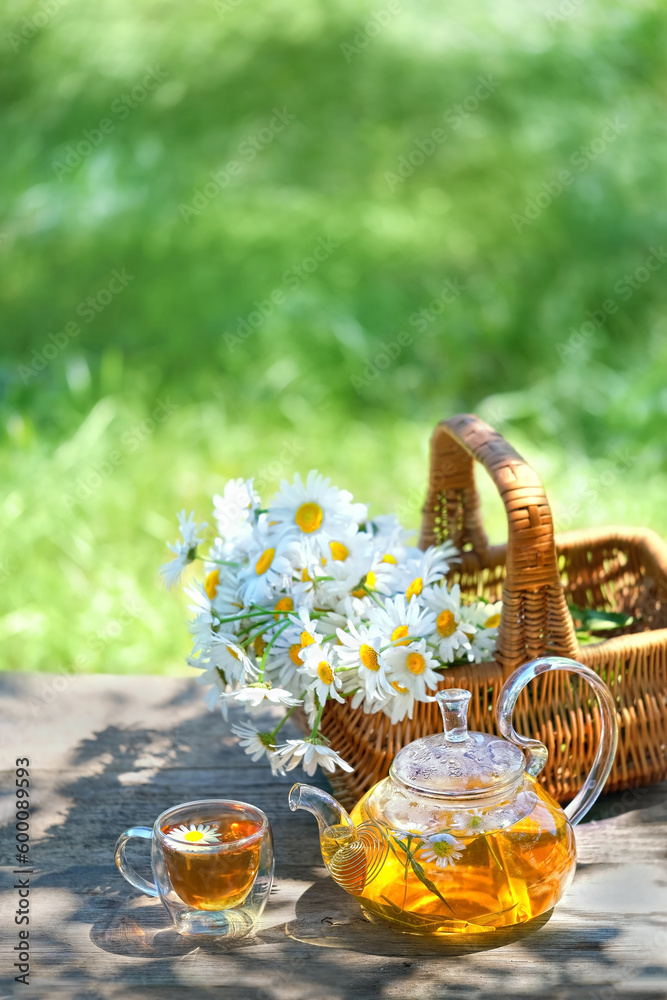 glass teapot, cup with herbal tea and Chamomile flowers in basket on ...