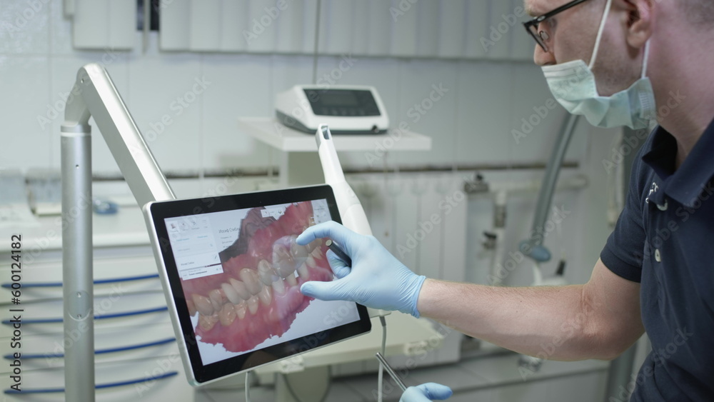 A professional dentist man looks at a 3d model of teeth on a computer ...