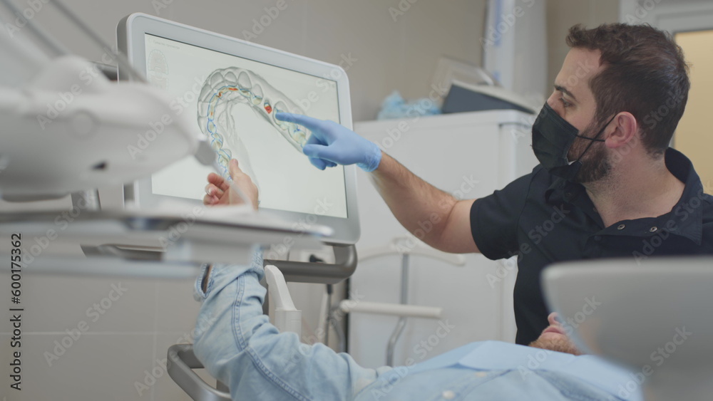 A male orthodontist doctor scans a man's teeth and jaw in the clinic's ...