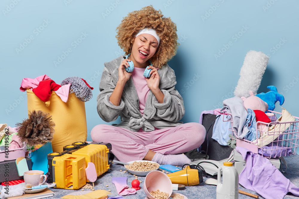 Positive housewife sings song feels glad sits in lotus pose on floor ...