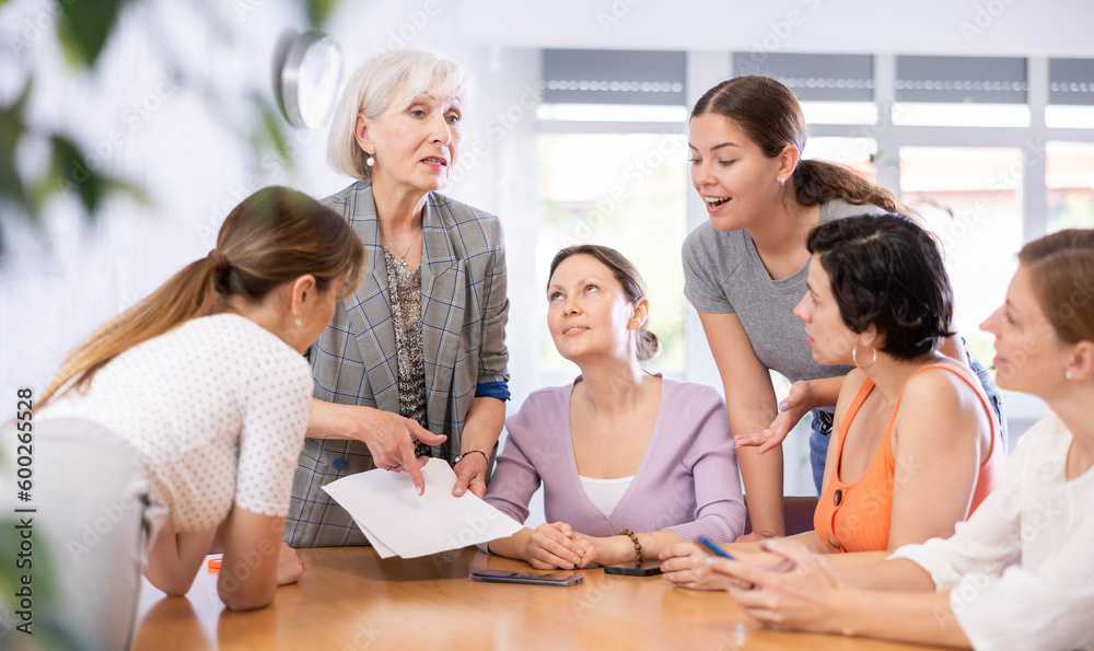 Group of friendly women of different ages sitting around table and ...