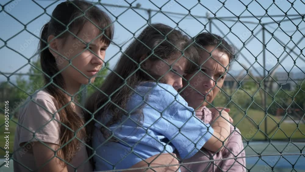 Desperate children hug their mother behind an iron mesh fence. Concept ...