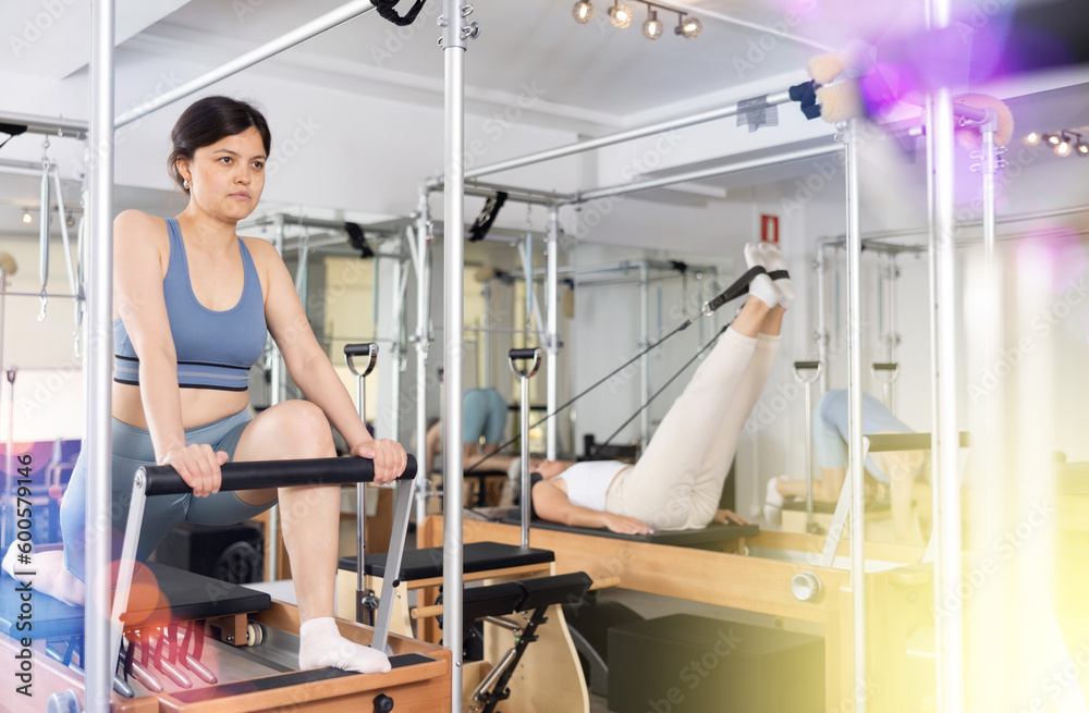 Focused young asian woman practicing exercises on Pilates reformer to ...