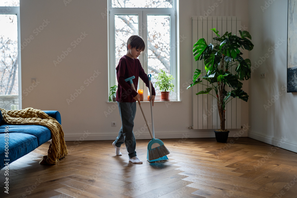 Teen boy doing chores cleaning floor in living room sweeping trash with ...