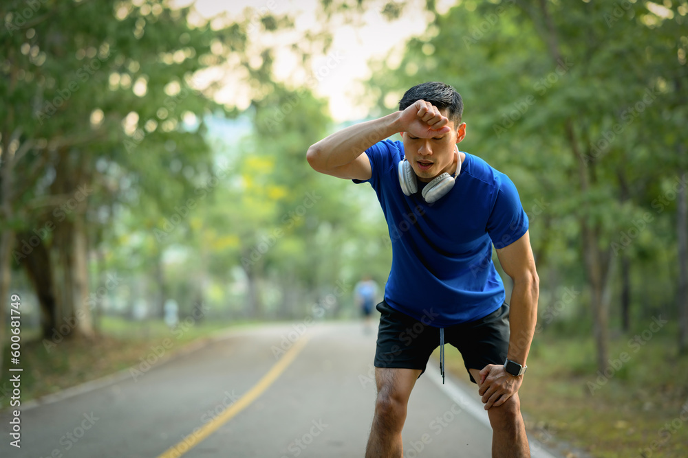 Shot of tired asian male athlete taking a break, resting after running ...