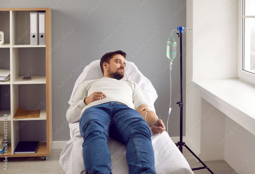 Young man lying in bed while receiving IV infusion in medical clinic ...