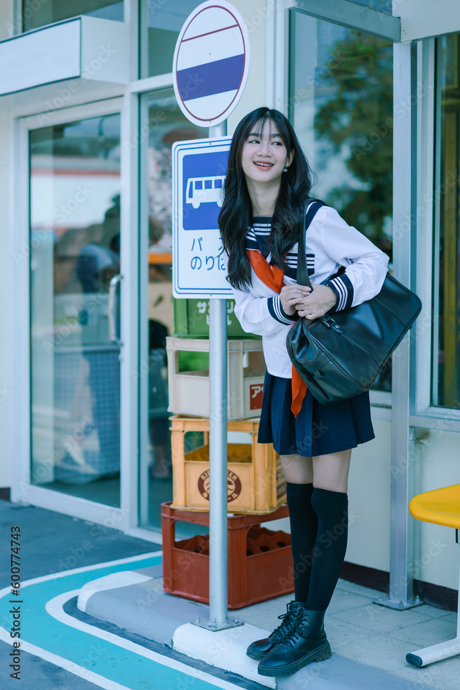 Cute Japanese schoolgirl in uniform downtown waiting at a bus station ...